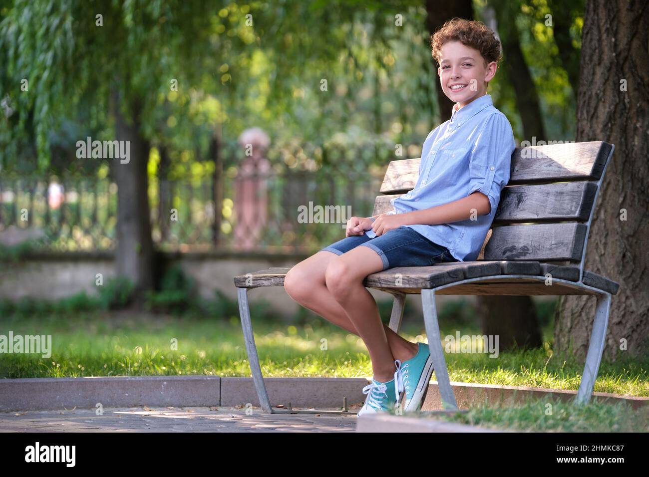 Young happy child boy relaxing sitting on bench in summer park ...