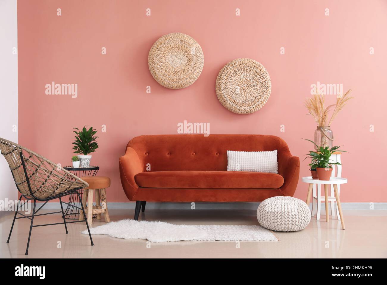 Stylish orange sofa with houseplants and wicker armchair in modern ...