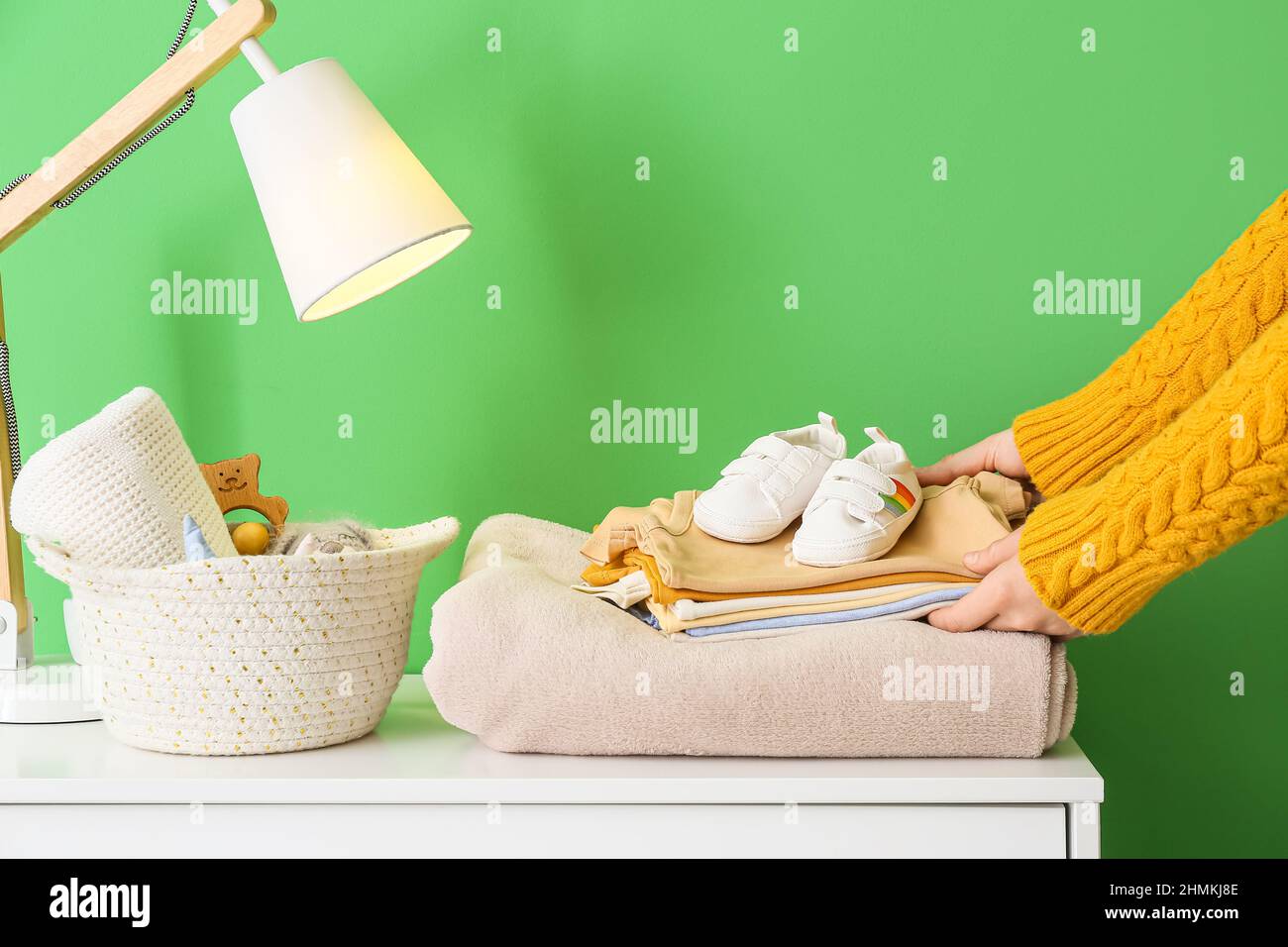 Woman taking baby clothes from chest of drawers near color wall Stock ...