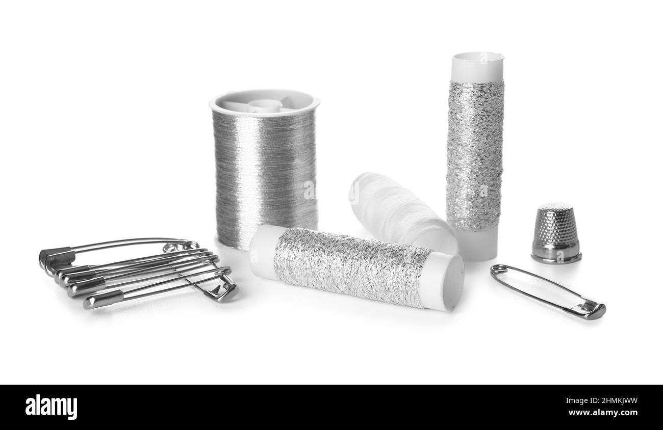 Different thread spools, thimble and safety pins on white background ...