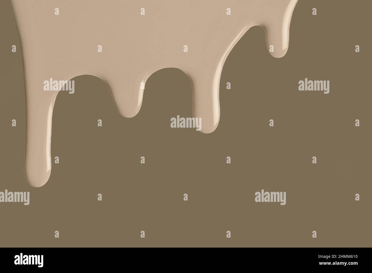 Beige liquid drops of paint color flow down on brown background ...