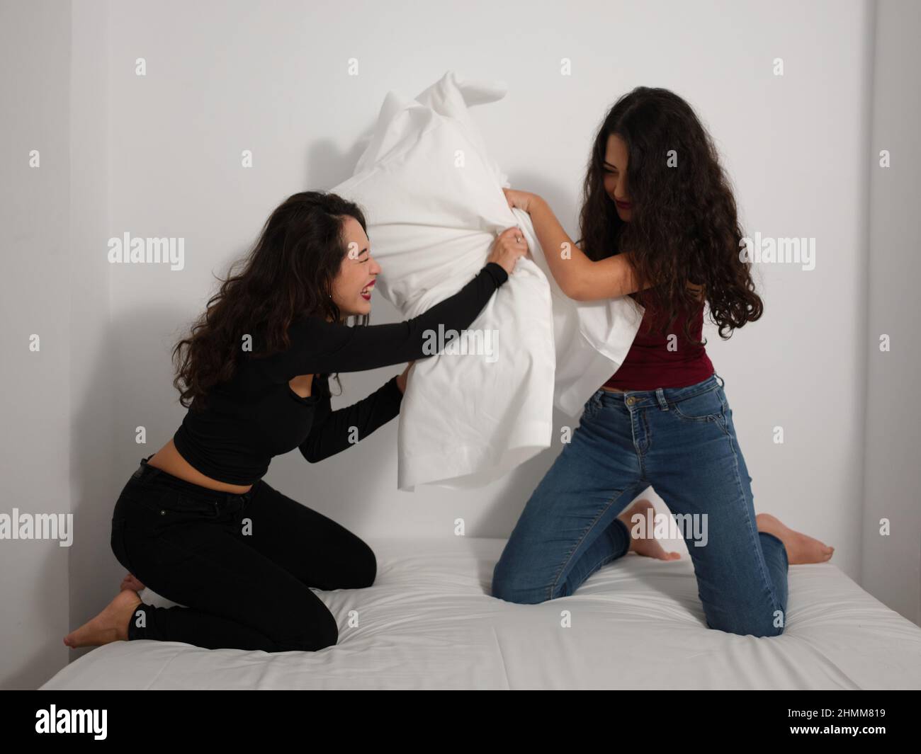 Two girls having fun playing pillow fight on the bed Stock Photo - Alamy