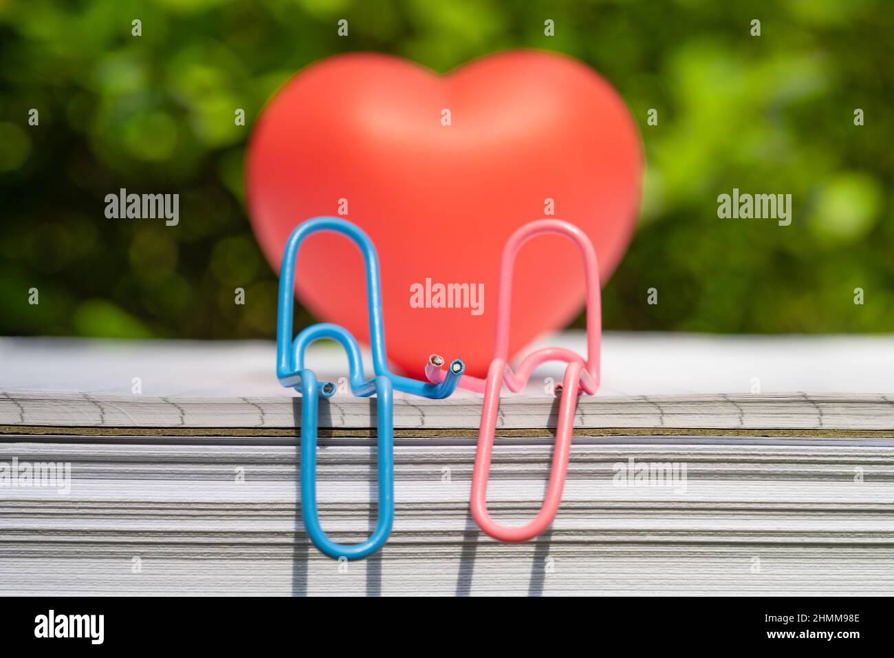 two paper clips shaped like lovers with a heart on background concept ...
