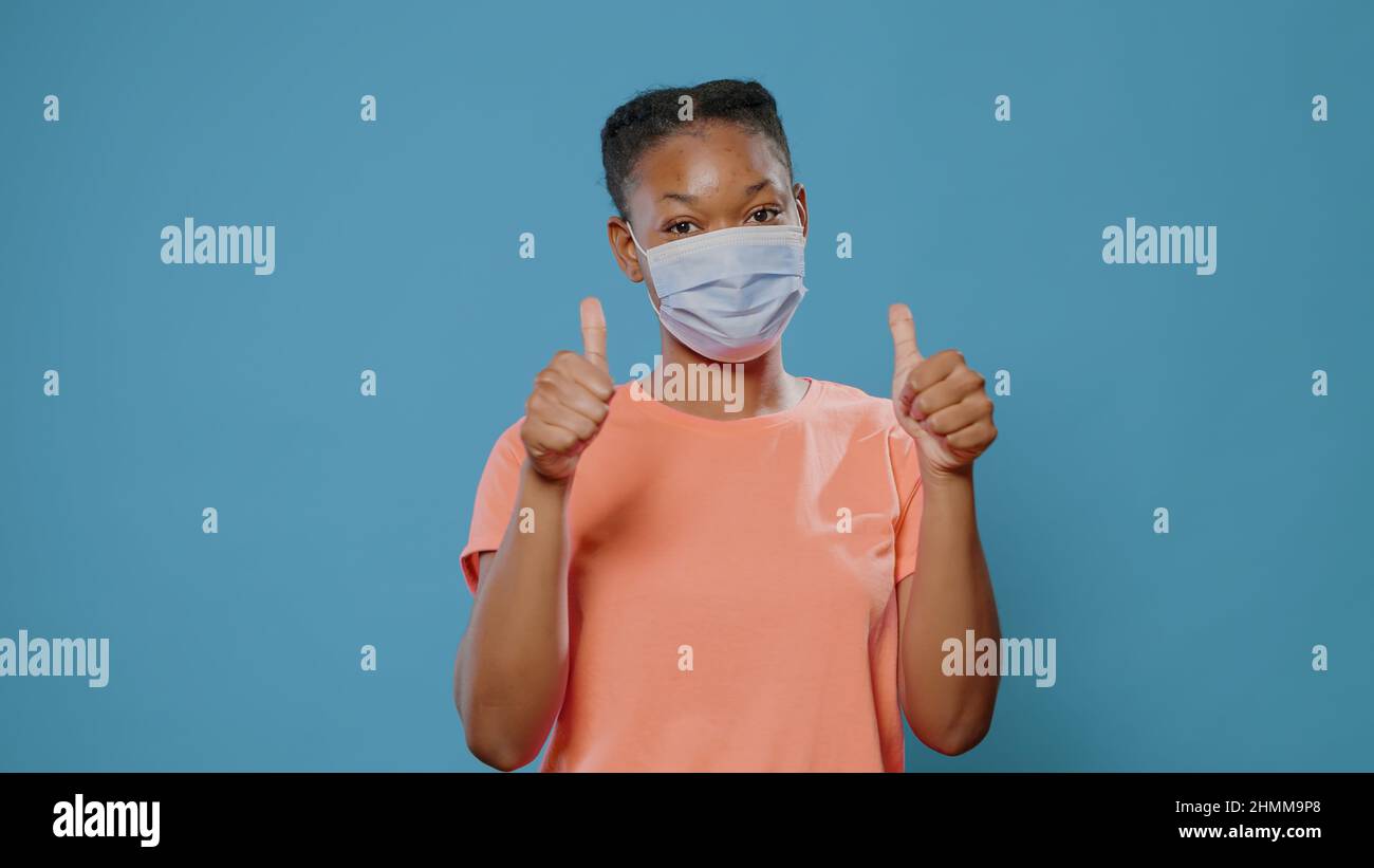 Portrait of casual person with face mask showing thumbs up sign in ...