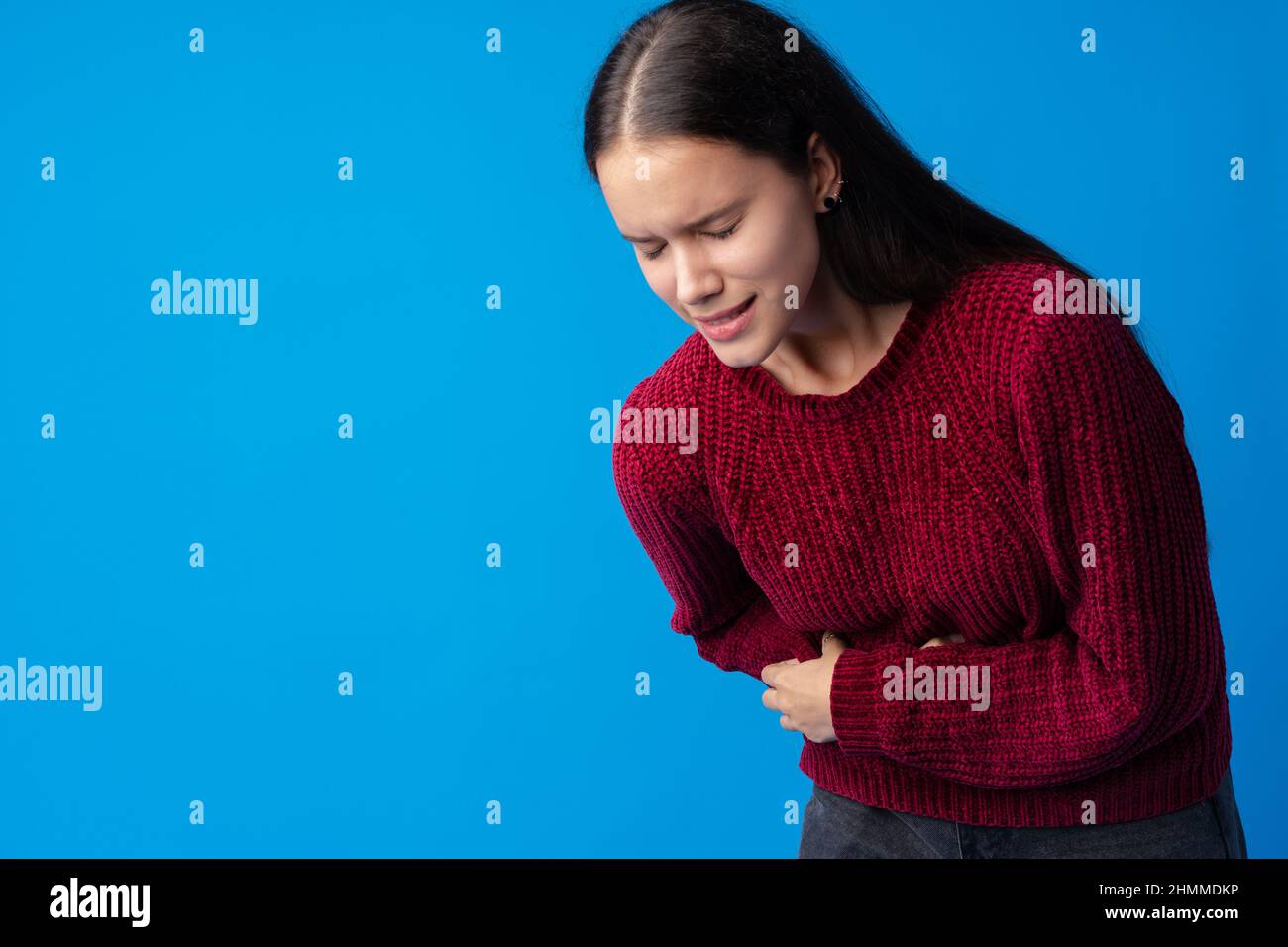 Young girl with bellyache isolated on a blue background Stock Photo - Alamy