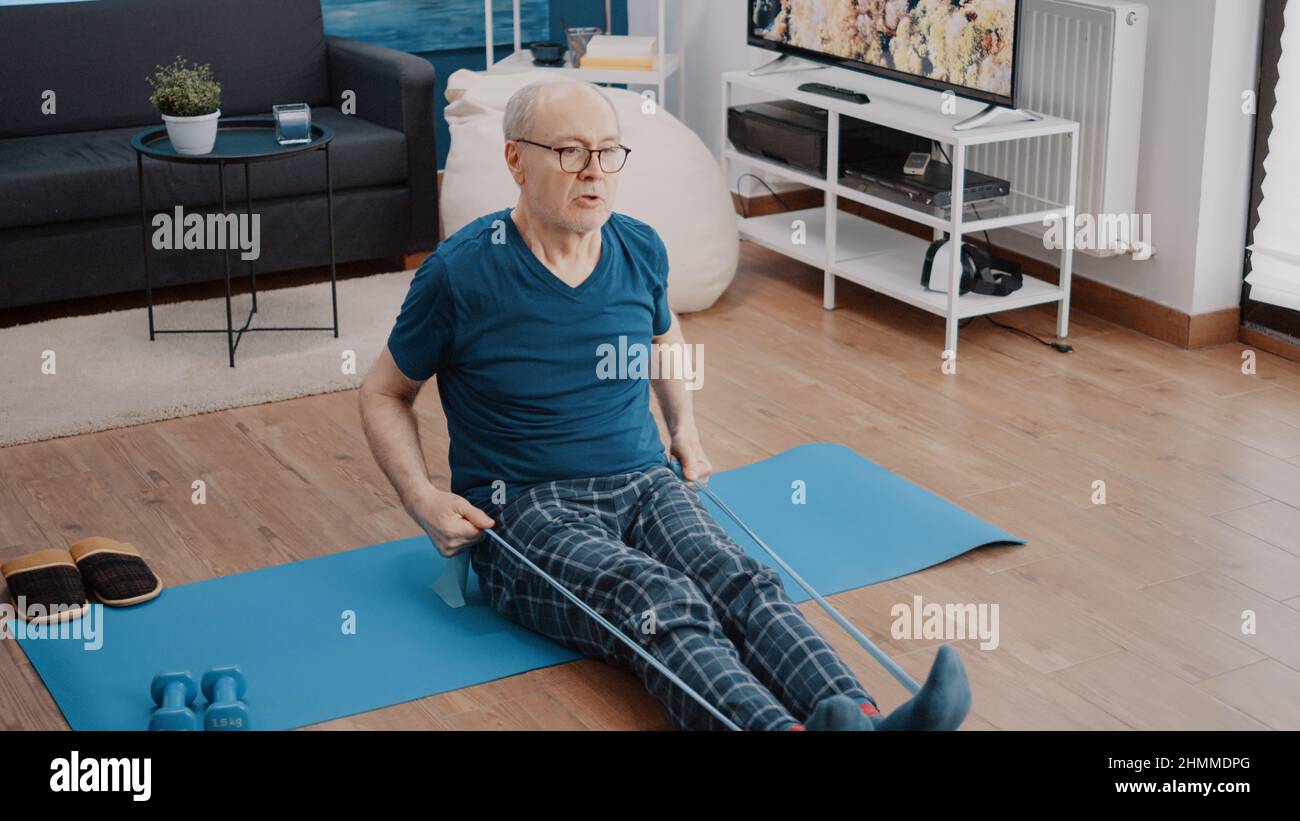 Pensioner using resistance band to stretch muscles on yoga mat. Senior ...