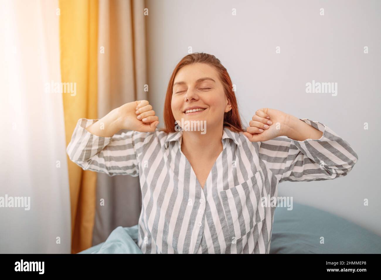 Beautiful young happy caucasian woman stretches after waking up in bed ...