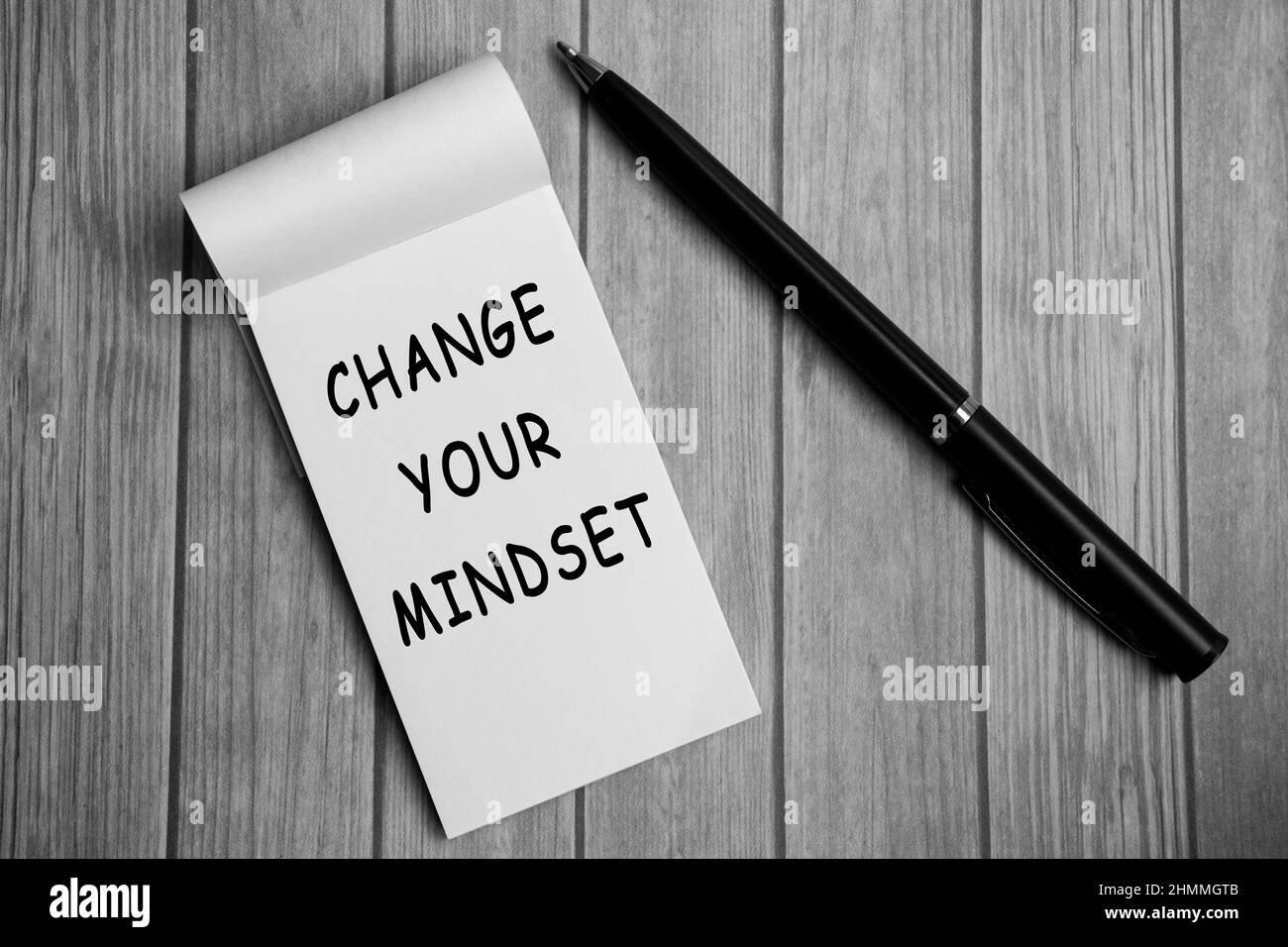 Change your mindset text on notepad and a pen on a wooden desk. Black and white background image ...