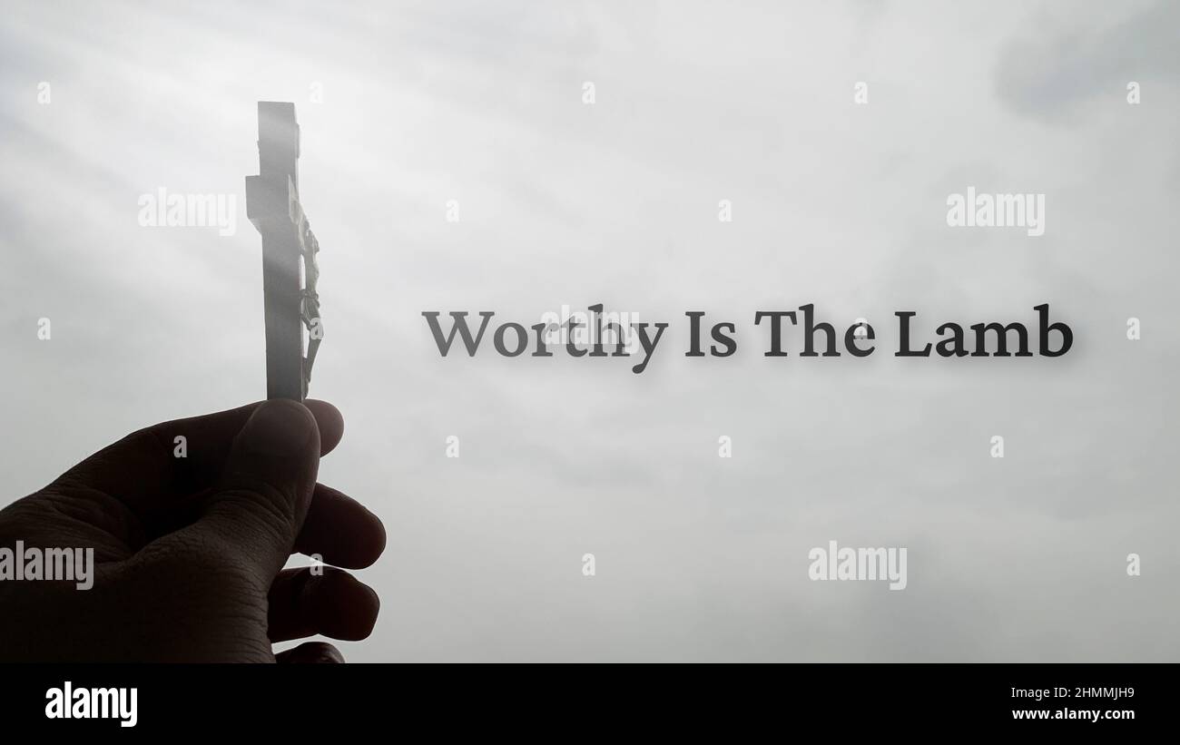 Hand holding Holy Cross with text - Worthy is the Lamb. With bright sky ...