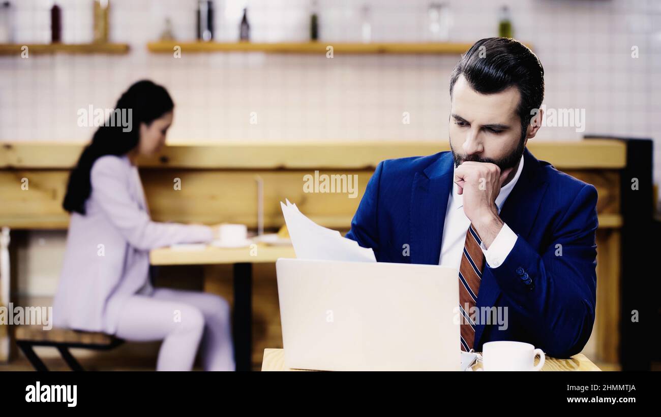 bearded businessman looking at papers near laptop and blurred ...