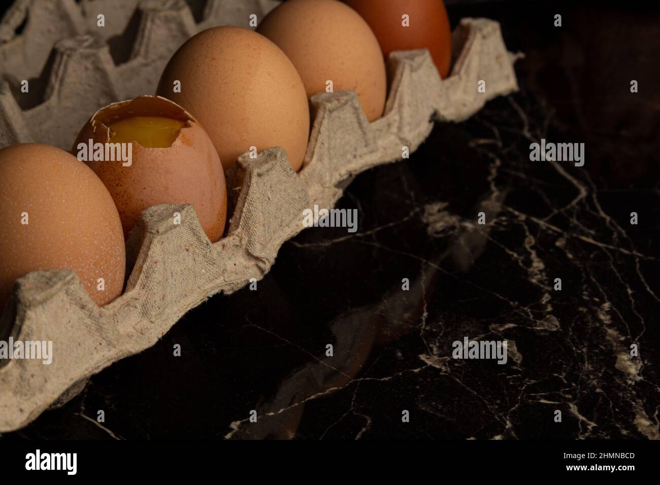 Fresh eggs and shells in an egg box, close-up on a dark marble ...