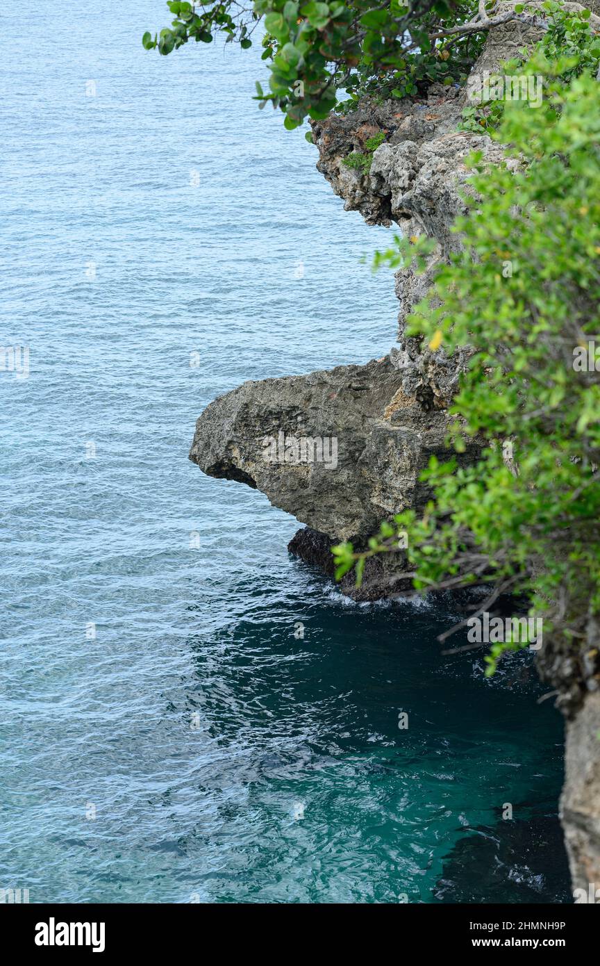 The photo shows a sheer cliff in the Caribbean Sea. The ocean water is ...