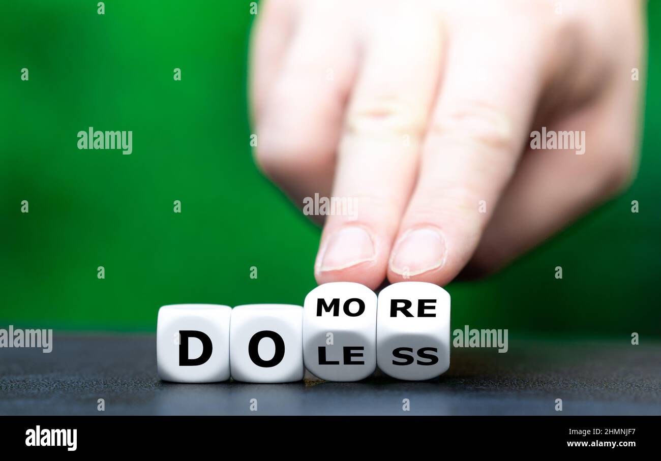 Hand turns dice and changes the expression "do less" to "do more Stock ...