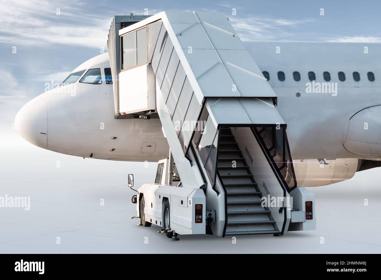 Passenger airplane with a boarding stairs on bright background with sky ...