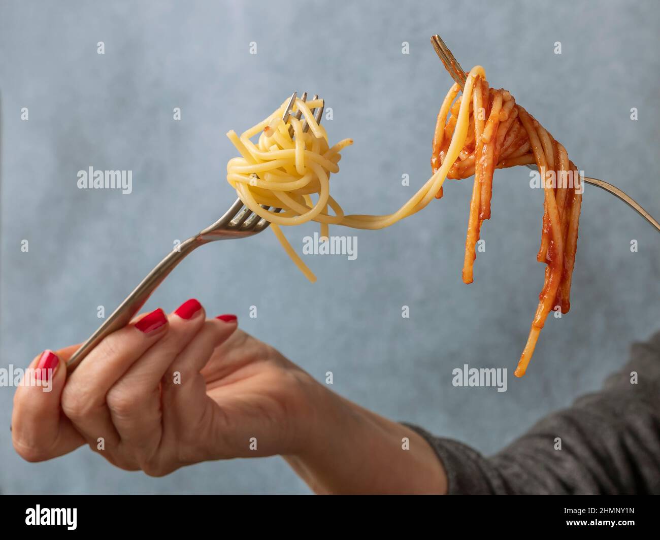 A woman's hands hold two forks with spaghetti in white on one side and ...