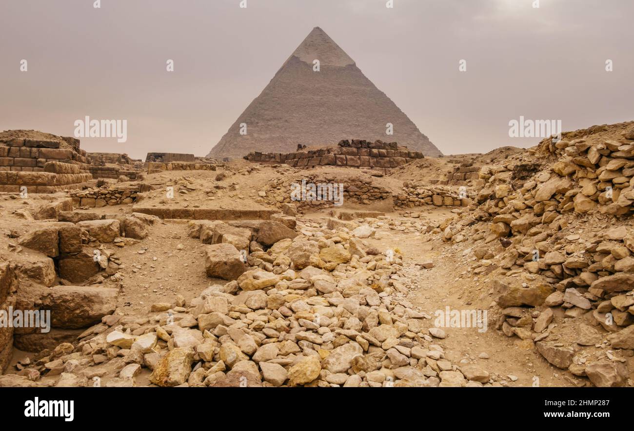 Excavations and ruins in desert against backdrop of pyramid and ...