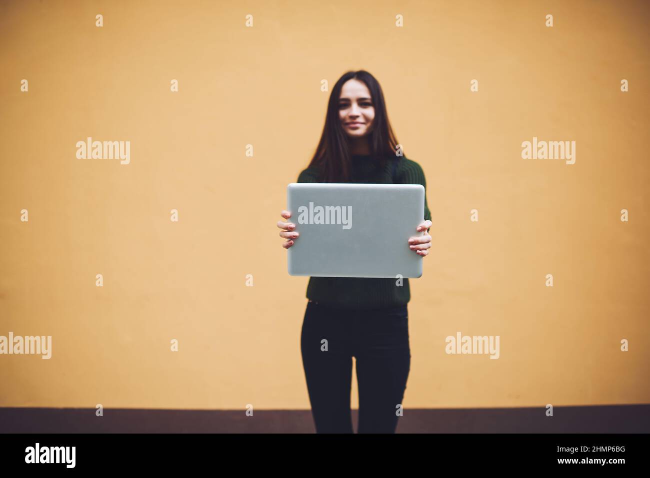 Female showing laptop while standing near wall Stock Photo - Alamy
