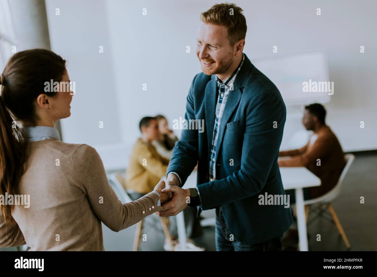 Young business partners making handshake in an office while their team ...
