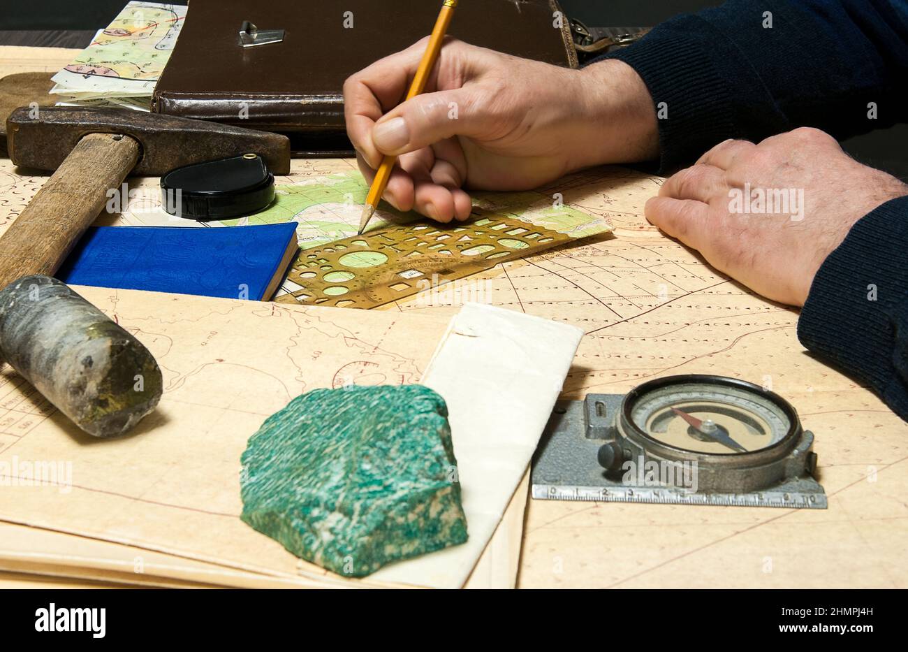 Geologist works with maps. On his desk are: map case, geological hammer ...