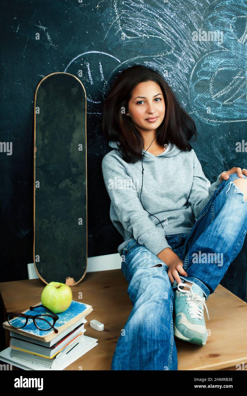 young cute teenage girl in classroom at blackboard seating on table ...