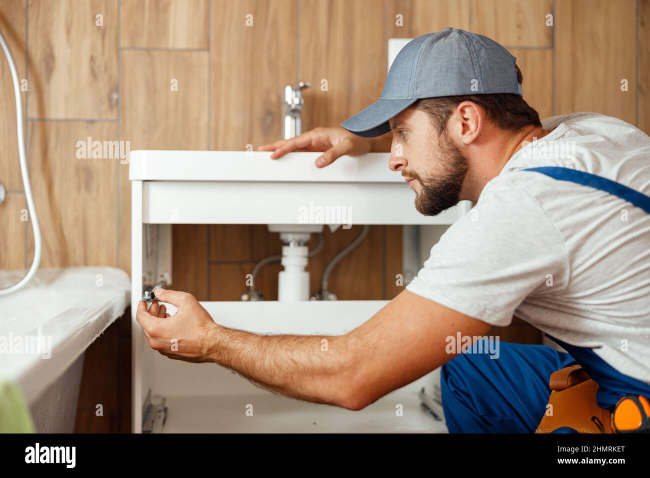 Concentrated plumber, male worker in uniform fixing sink and water pipe ...