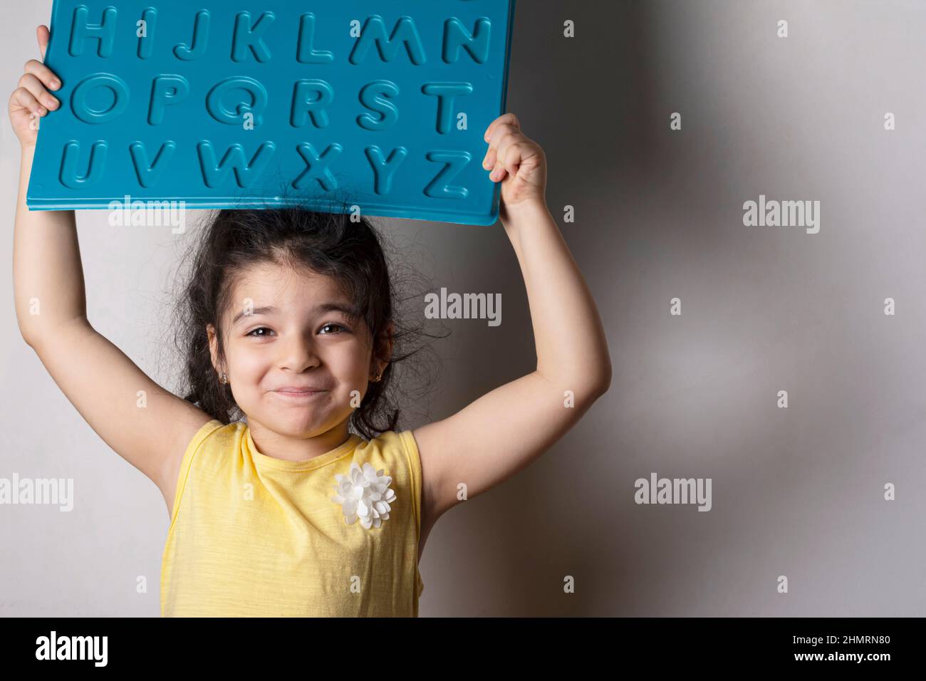 Little girl with yellow dress rising English letters sheet on upper ...