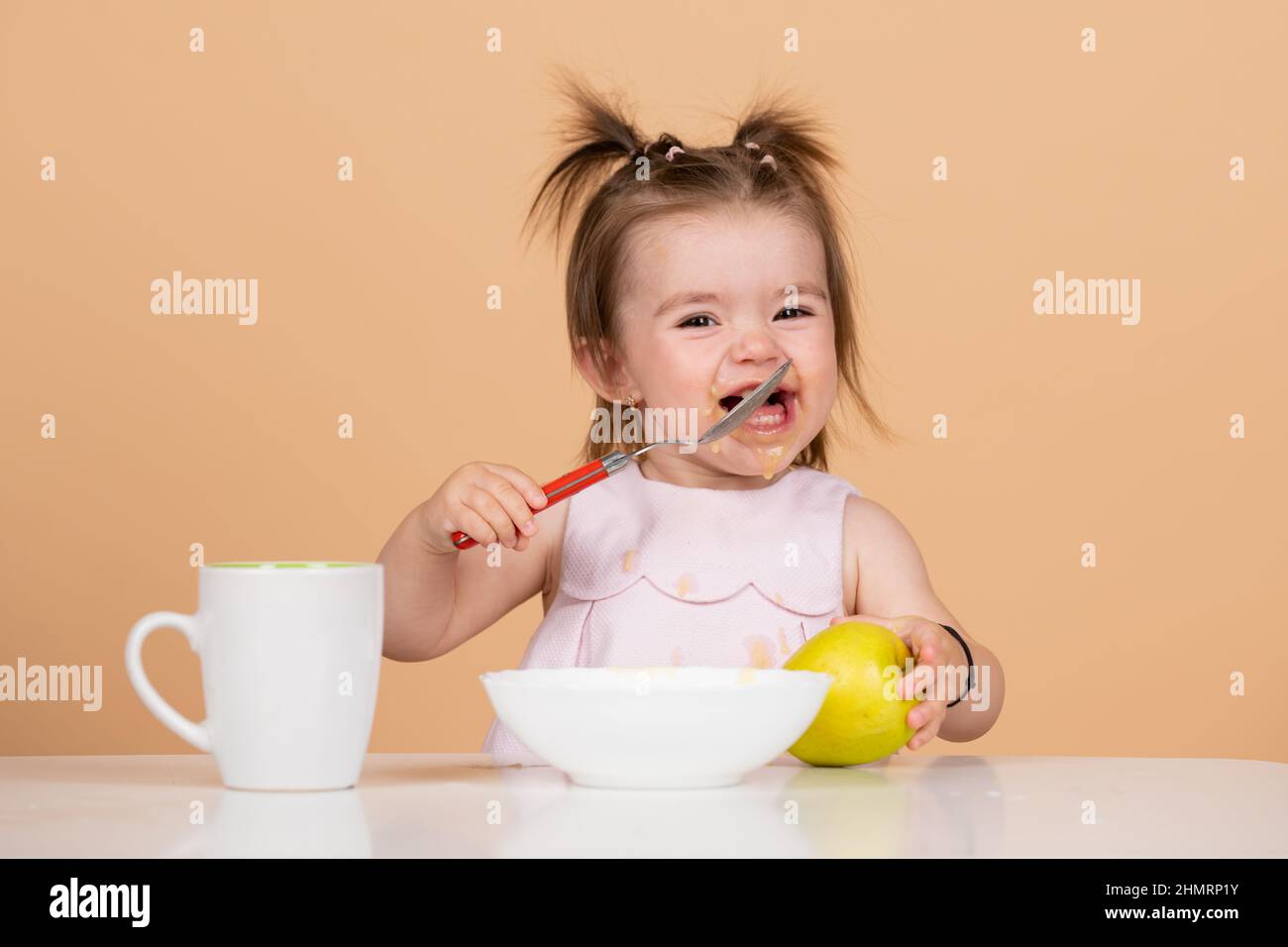 Baby child eating food. Happy smiling baby girl with spoon eats itself ...
