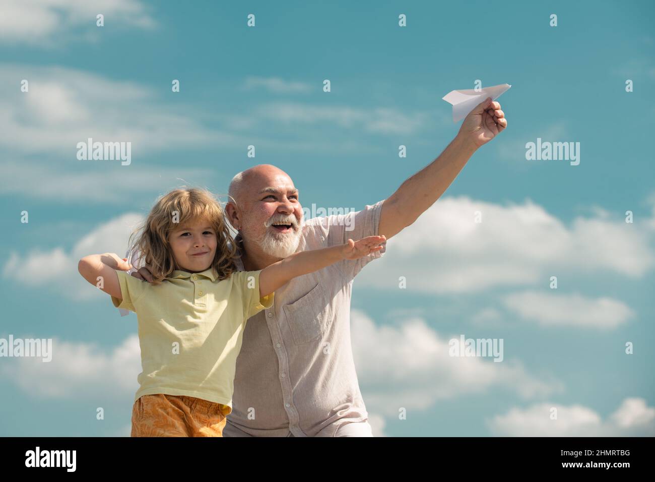 Grandfather and grandson playing with paper plane against summer sky ...