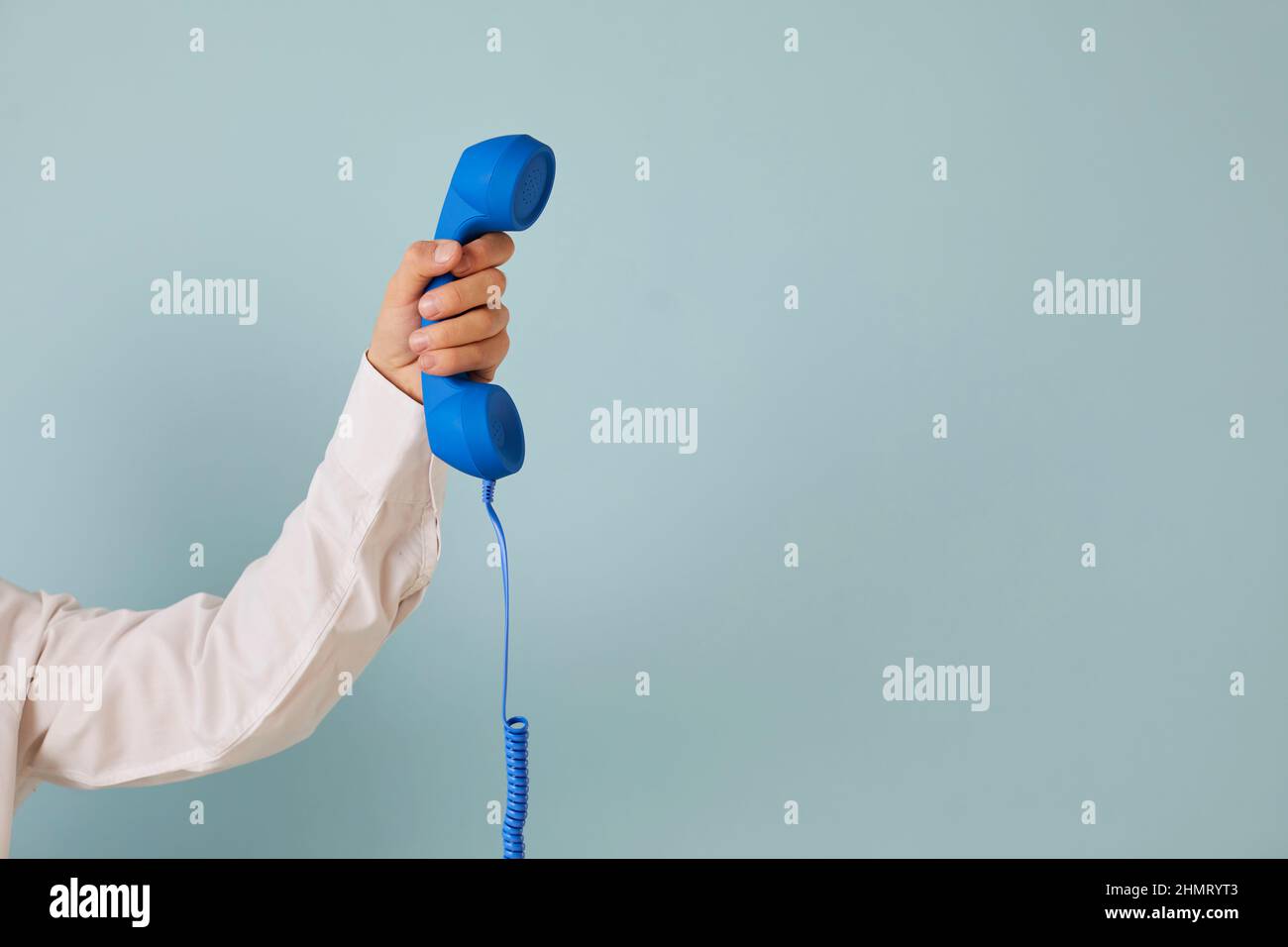 Human hand holding blue landline phone receiver on light blue copy ...