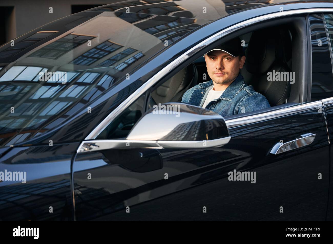 Portrait of male driver in cap sitting in electric car. Handsome young ...