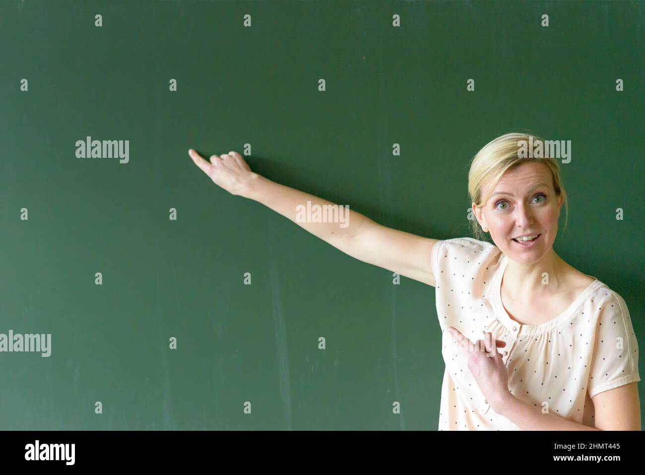 Female teacher pointing at copy space place on chalkboard, looking at ...