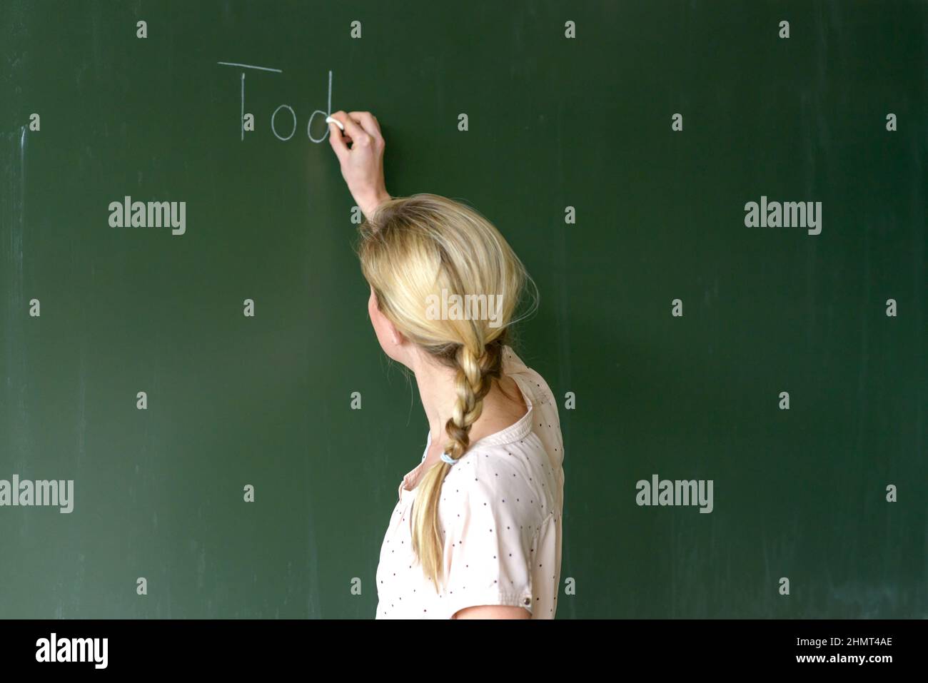 Female teacher with blond hair ponytail writing with chalk on top of a ...