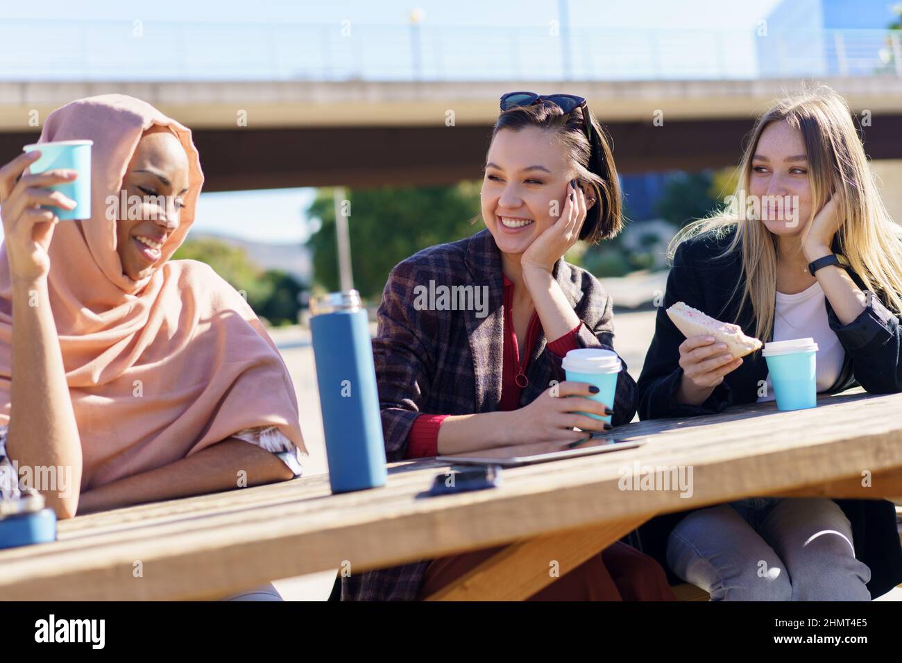Cheerful diverse ladies having coffee break and chatting in city park ...