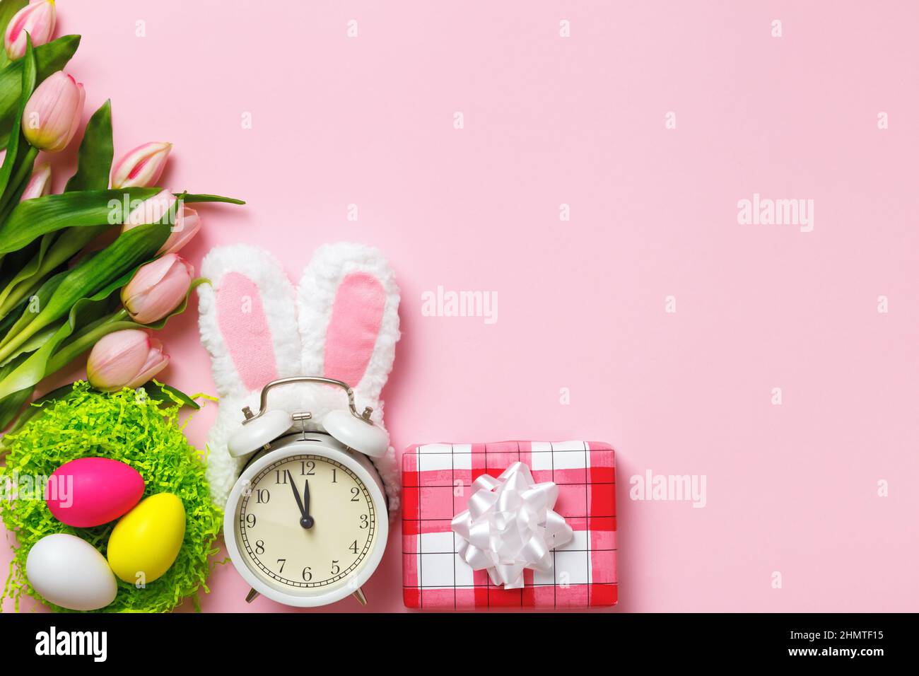 Easter card. Alarm clock rabbit ears gift eggs flowers tulips on a pink ...