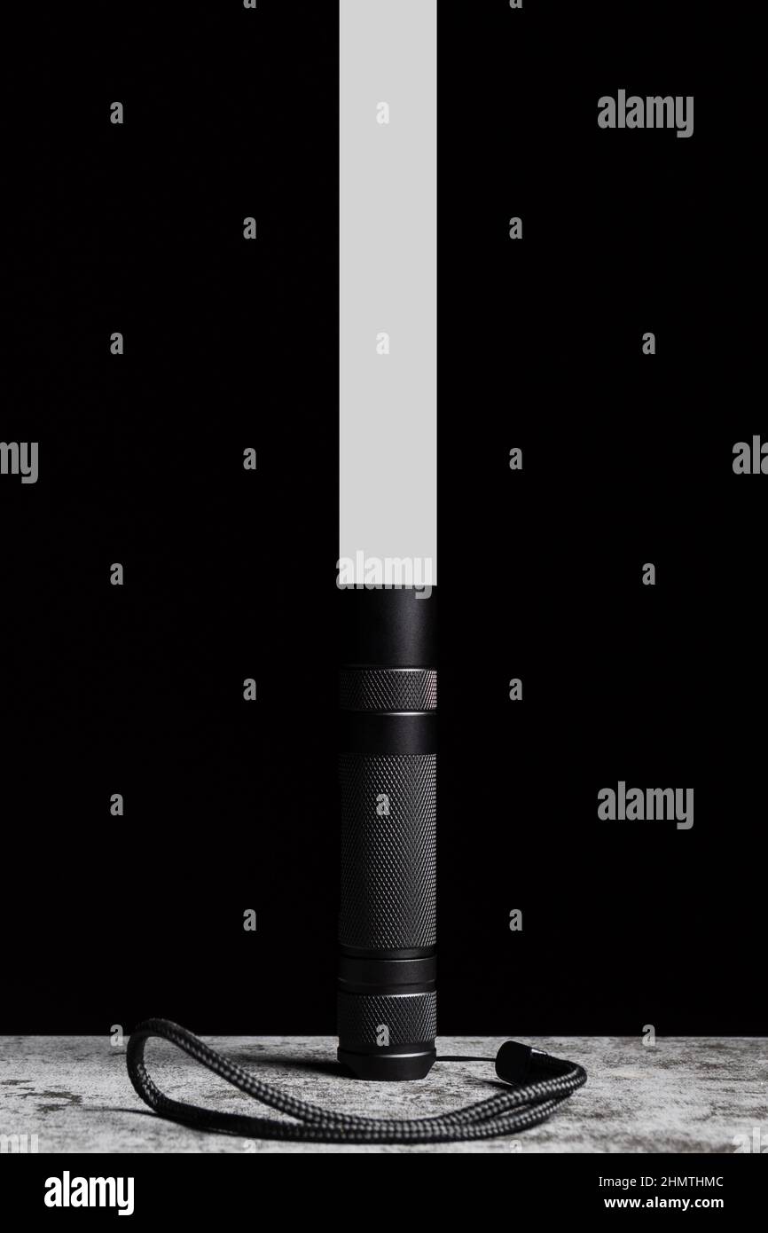 Flashlight stands on a table with a narrow beam of light upwards on a ...