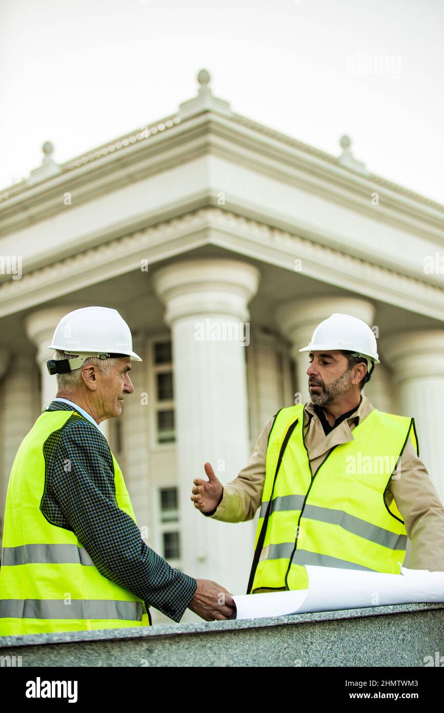Two senior construction workers are having a conversation about the new ...