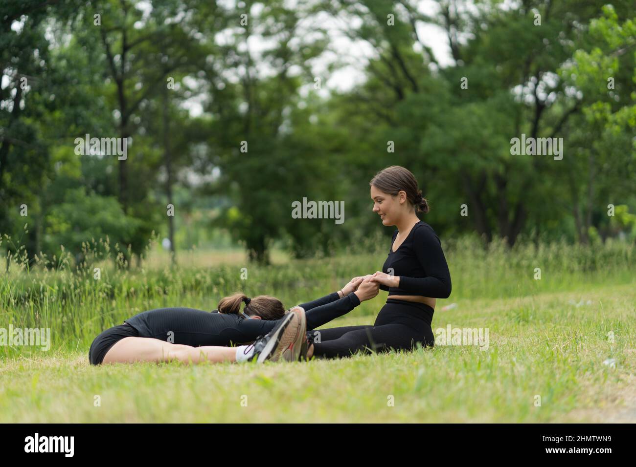Two attractive girls are helping each other to stretch while sitting on ...