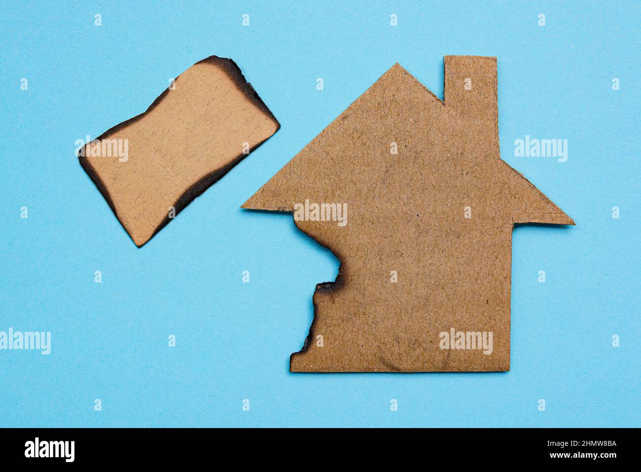 Burned paper house model on blue background. Home insurance concept ...