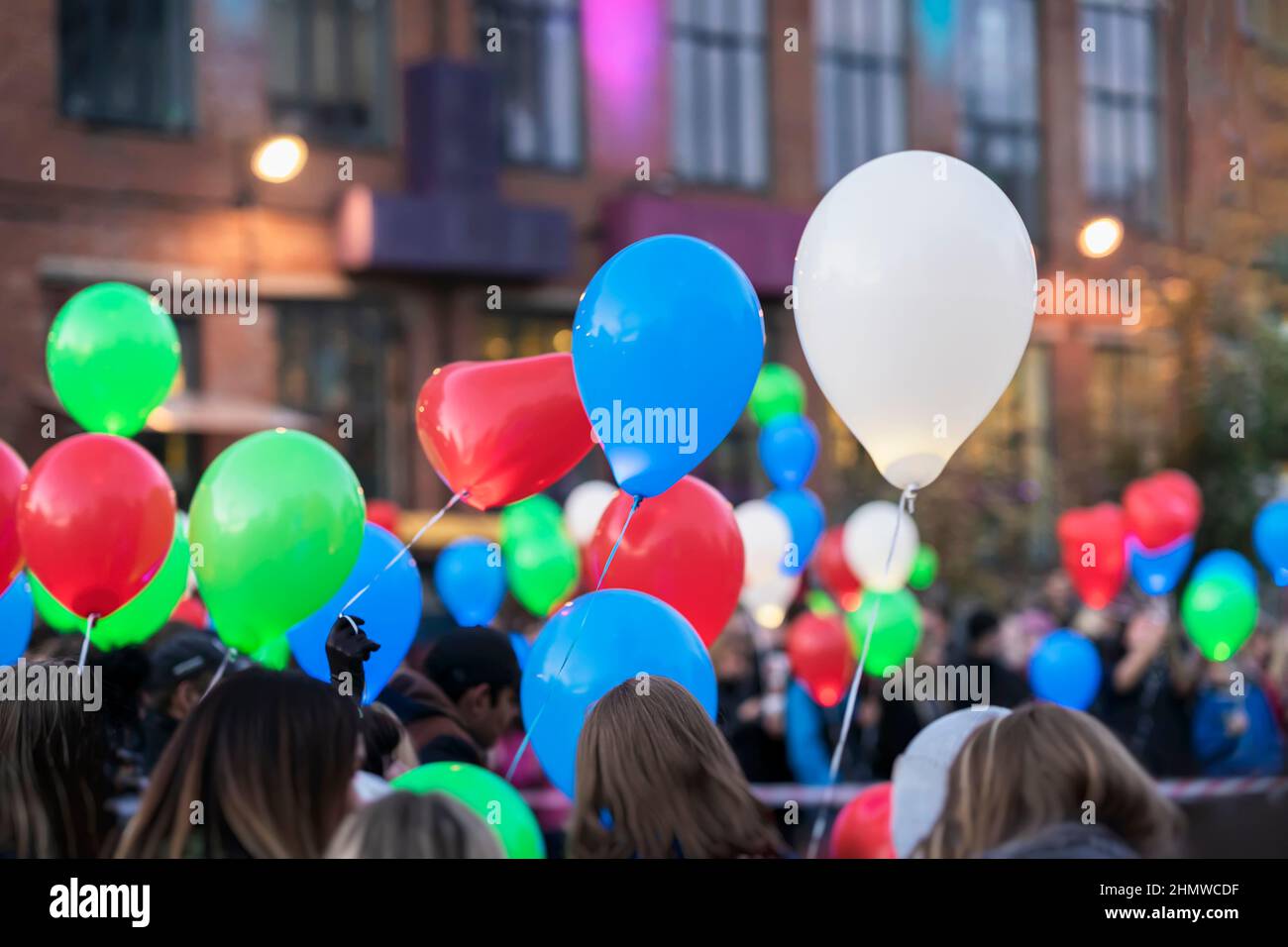 Many colorful balloons in hands of crowd of celebrating people at night ...
