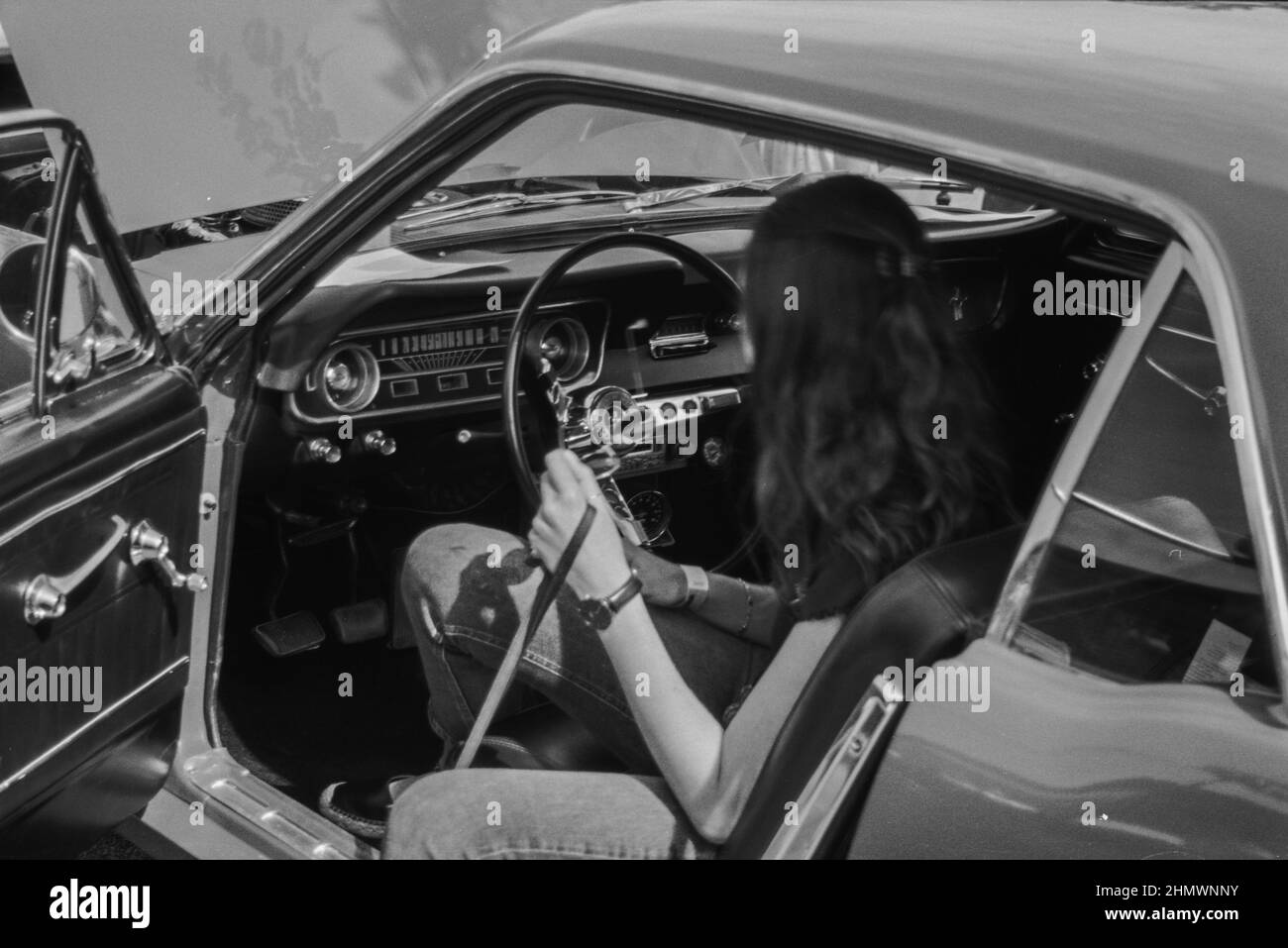 Grayscale shot of a young woman on the old classic Ford Mustang car in ...
