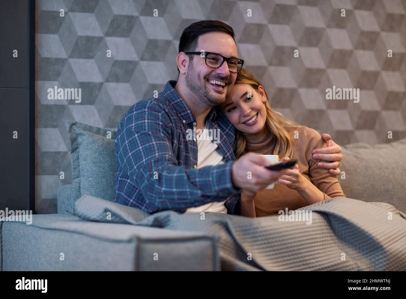 Smiling man and woman are hugging while relaxing at home and watching ...