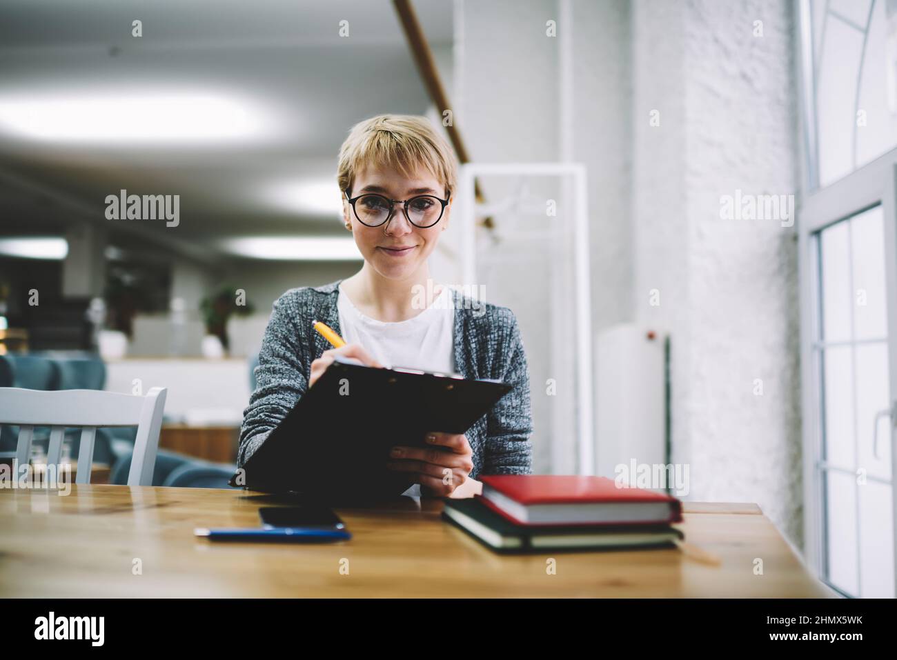 Smiling female writing report while working Stock Photo - Alamy
