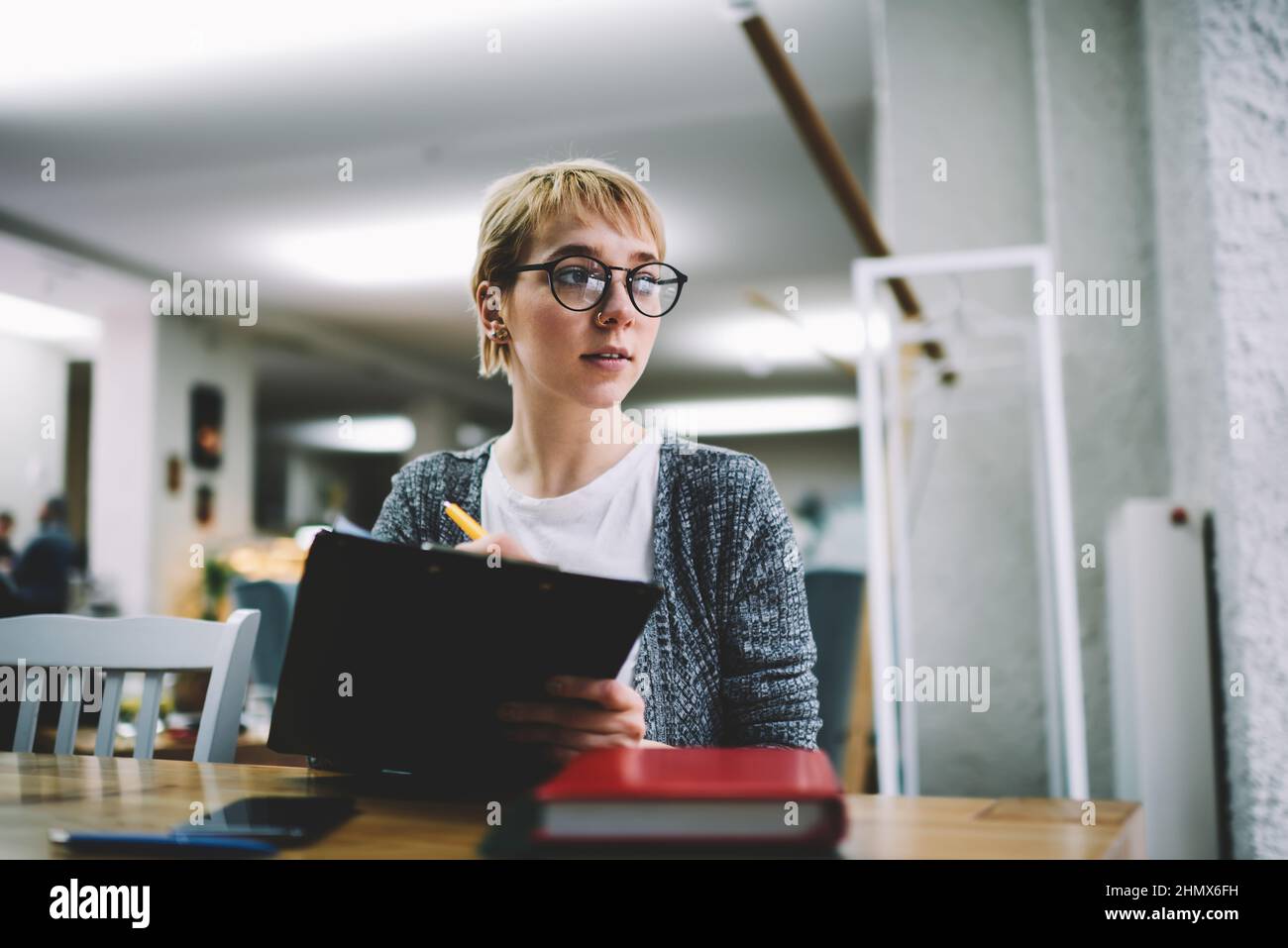 Pensive woman with clipboard working in modern workspace Stock Photo ...