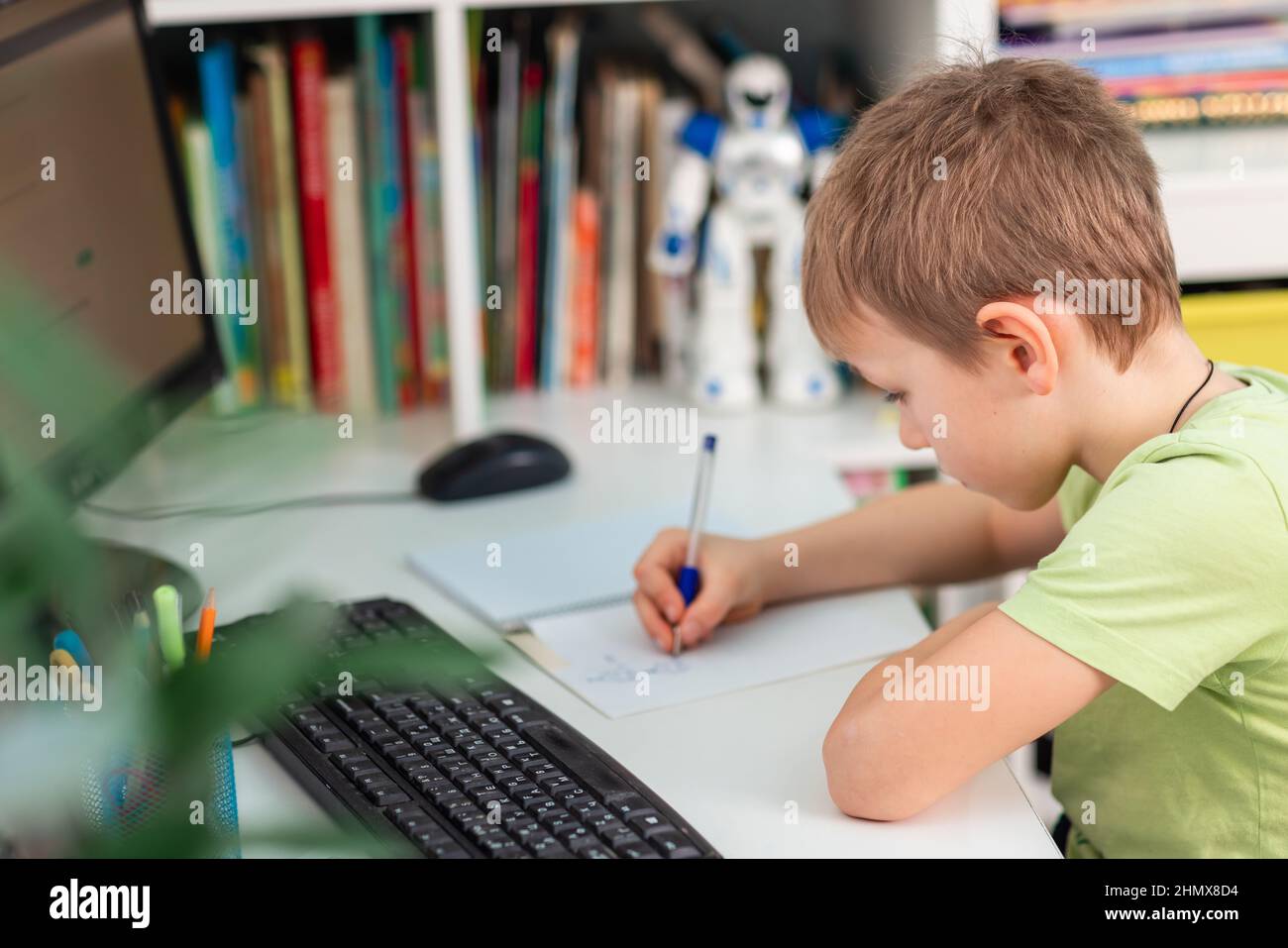 Little young school boy working at home with a laptop and class notes ...
