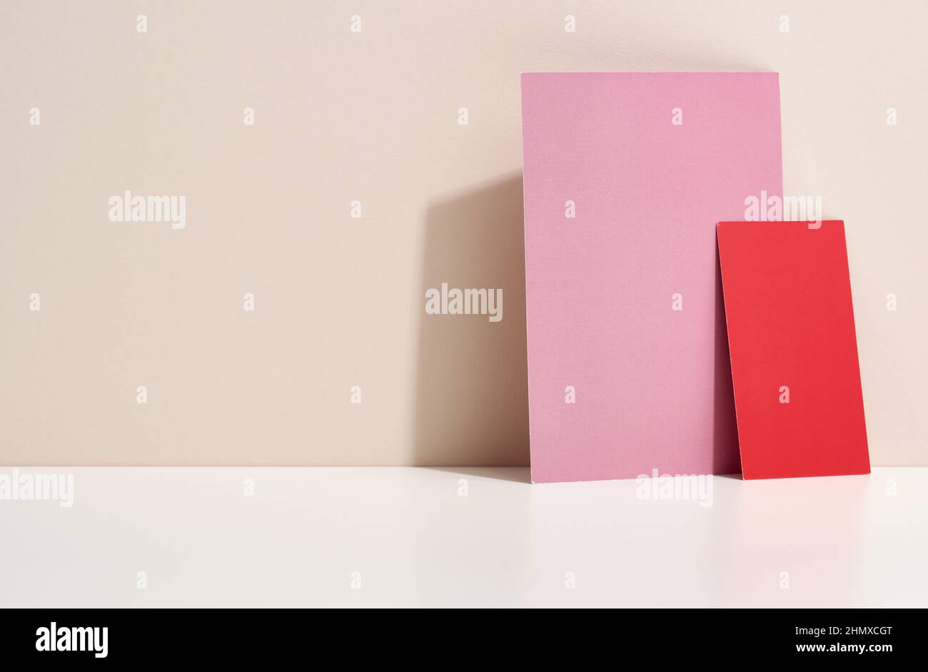 blank pink and red cardboard sheet of paper with shadow on white table ...