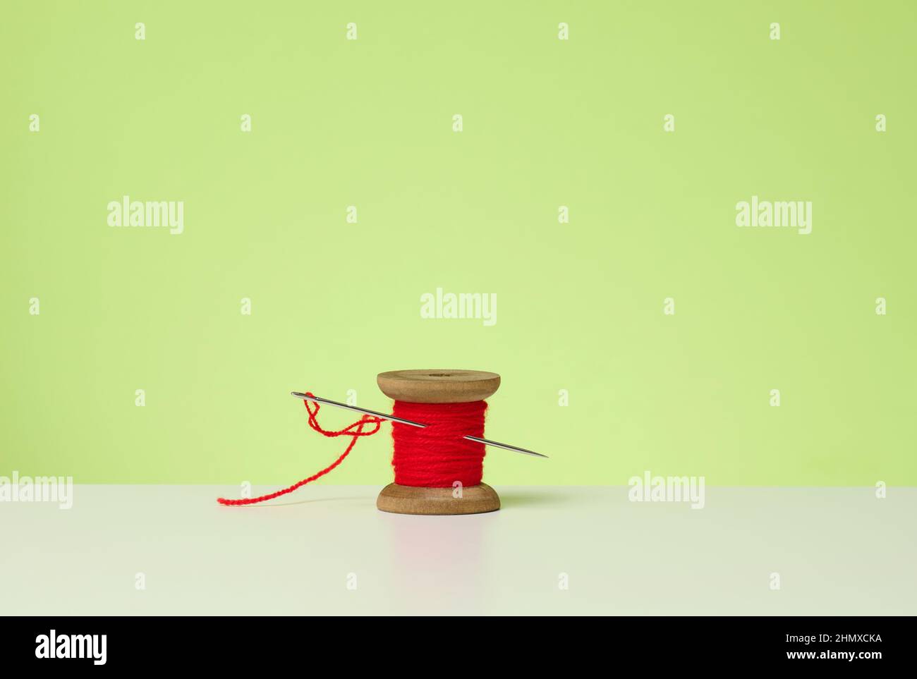 wooden spool with red wool thread and a large needle on a white table ...
