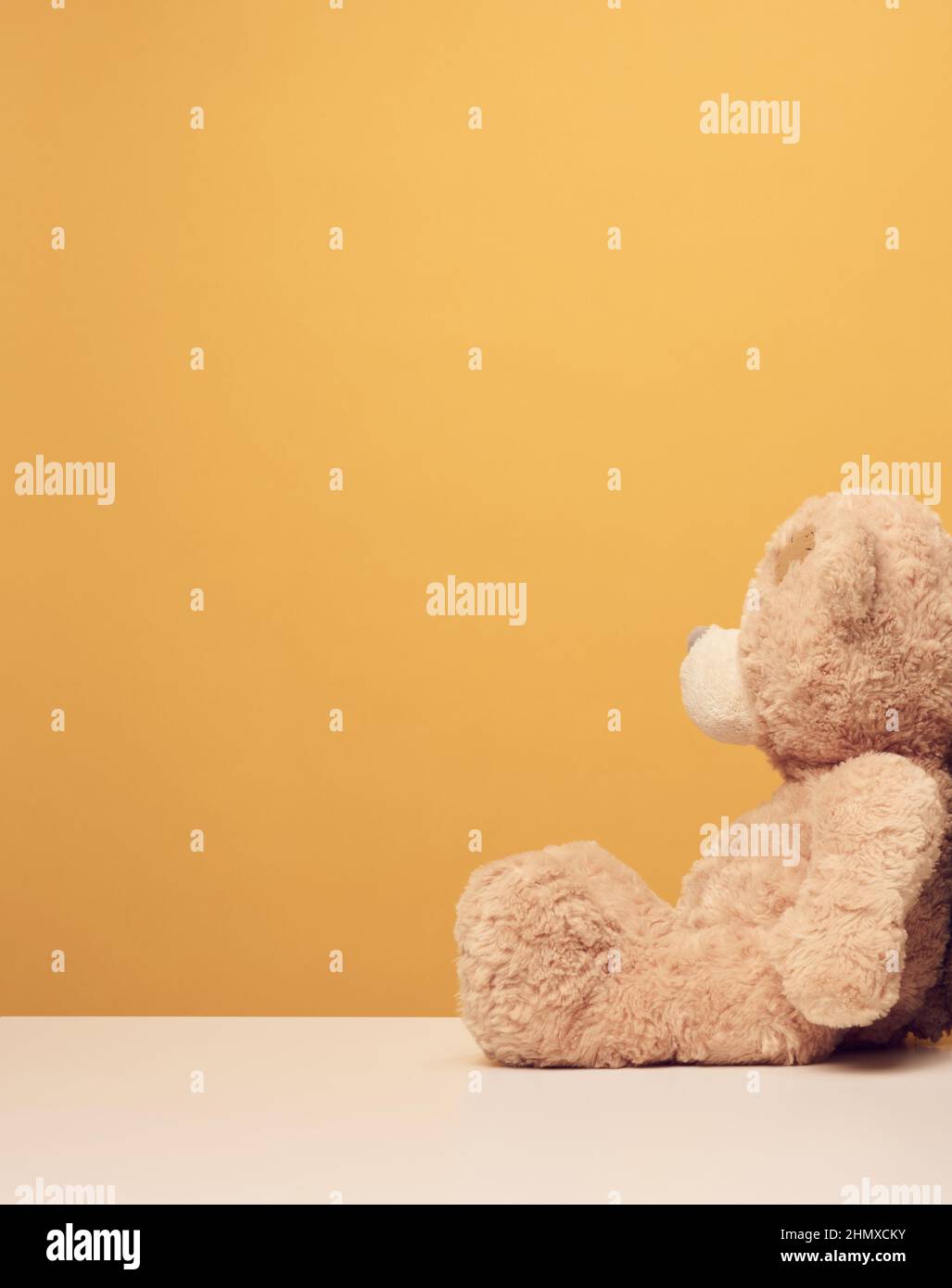 brown cute teddy bear sits sideways on yellow background, sadness Stock ...
