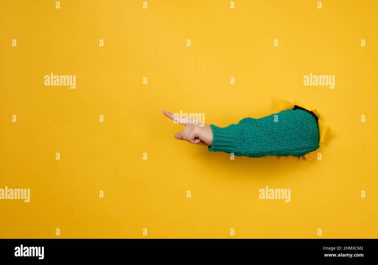 female hand sticks out of a torn hole in a yellow paper background ...