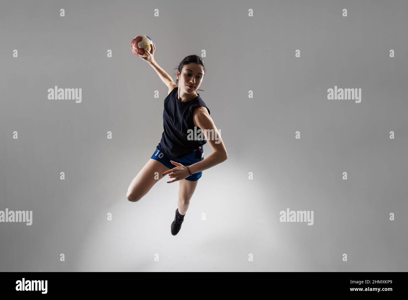 Handball player posing on light gray background. Girl jumping with ball ...
