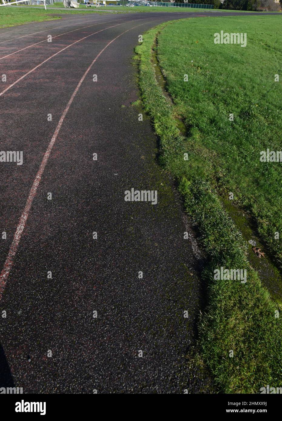 An old, worn and overgrown with grass running track in a school field ...